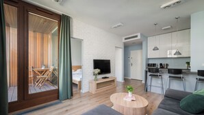 Uma sala de estar moderna com televisão, sofá e mesa de centro. Há uma varanda com deck de madeira e porta de correr.