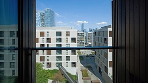 Vista pela janela de um edifício moderno com vários andares e varandas, sob um céu claro.