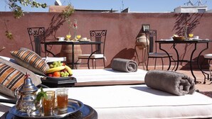 Terraço no telhado com mesa para dois, um sofá e uma toalha enrolada, além de bandeja com frutas e bebidas.