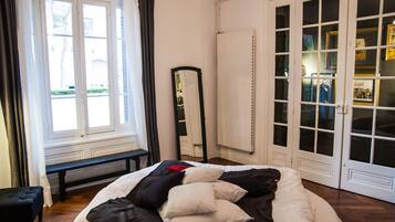 Quarto com cama, um banquinho, espelho e guarda-roupa com portas de vidro.
