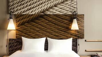 Quarto de hotel com cama, duas luminárias de cabeceira, mesa de cabeceira e cabeceira com design texturizado.