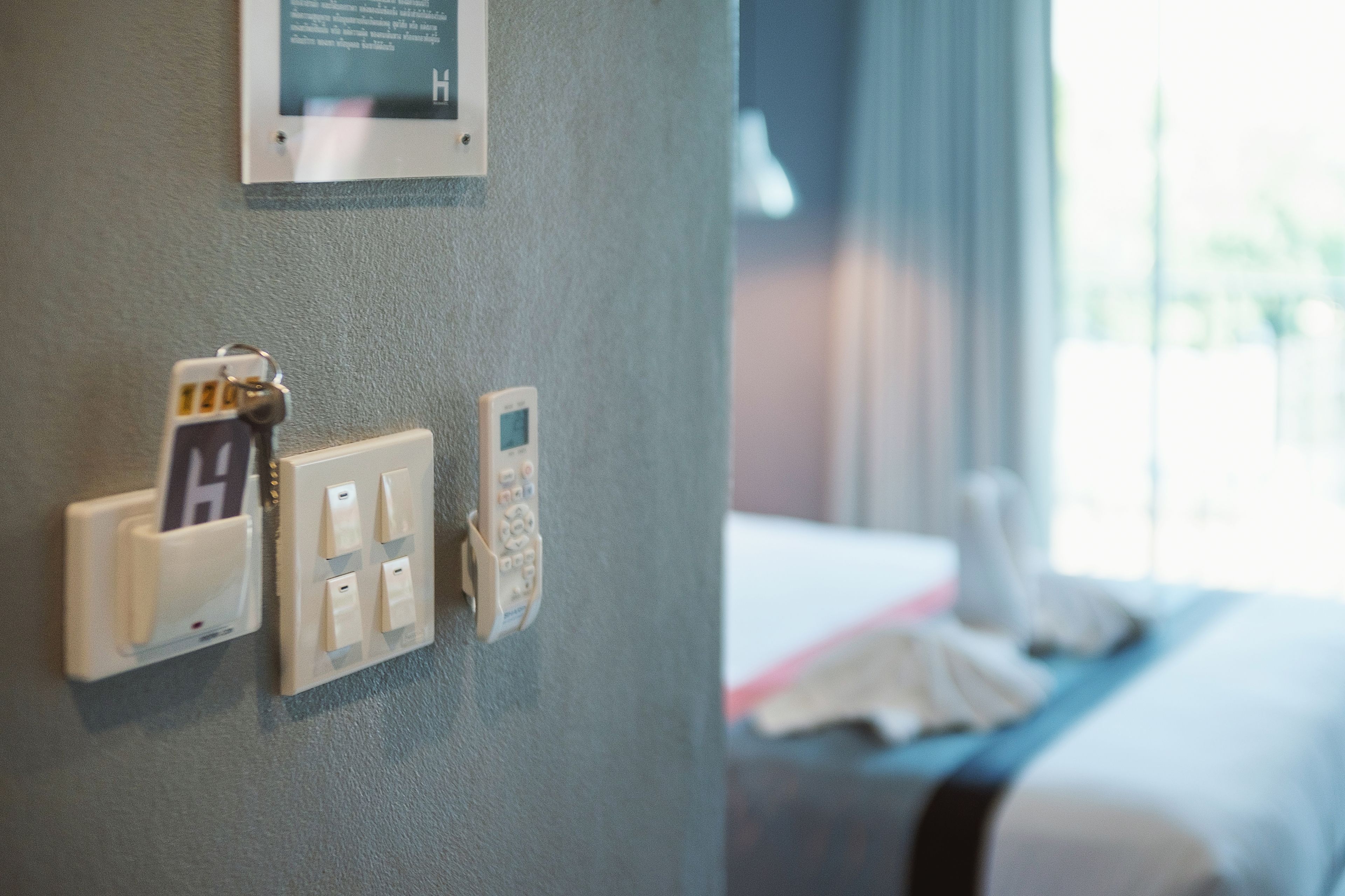 Quarto de hotel com uma cama, um telefone fixado na parede e um porta-chaves.