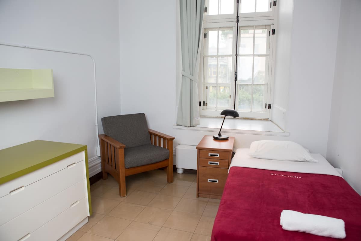Quarto com cama, cadeira, escrivaninha e janela.