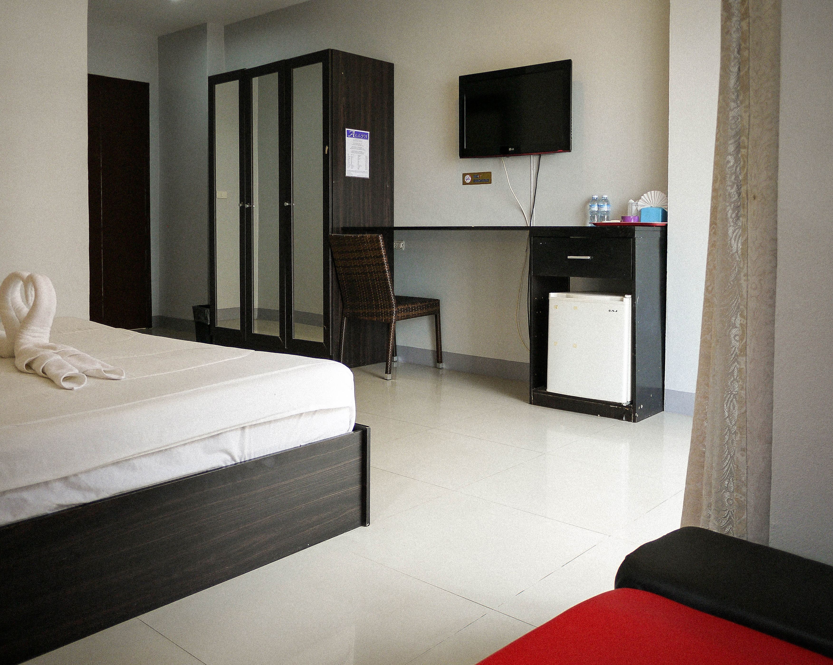 Quarto de hotel com cama, escrivaninha com televisão, cadeira e pequeno frigorífico.