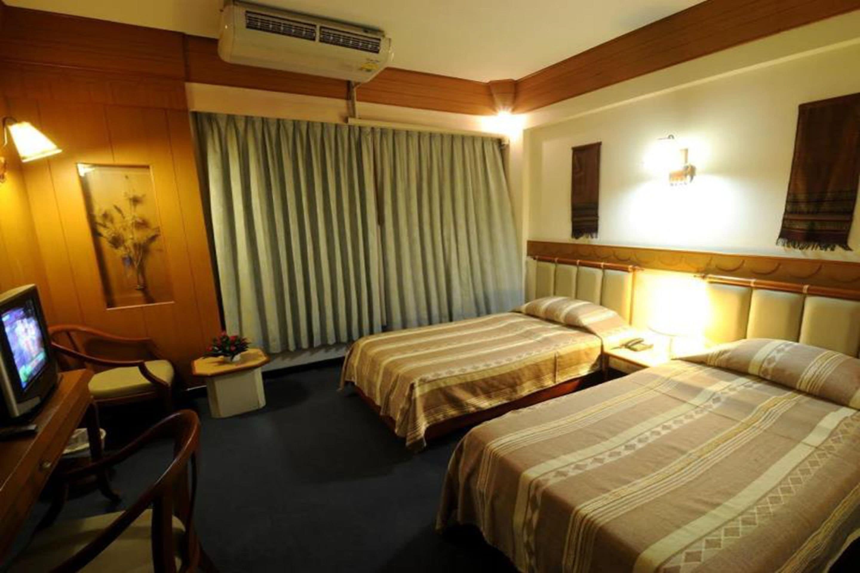 Quarto de hotel com duas camas, uma escrivaninha com computador, uma cadeira e ar-condicionado na parede.