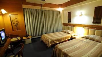 Quarto de hotel com duas camas, uma escrivaninha com computador, uma cadeira e ar-condicionado na parede.