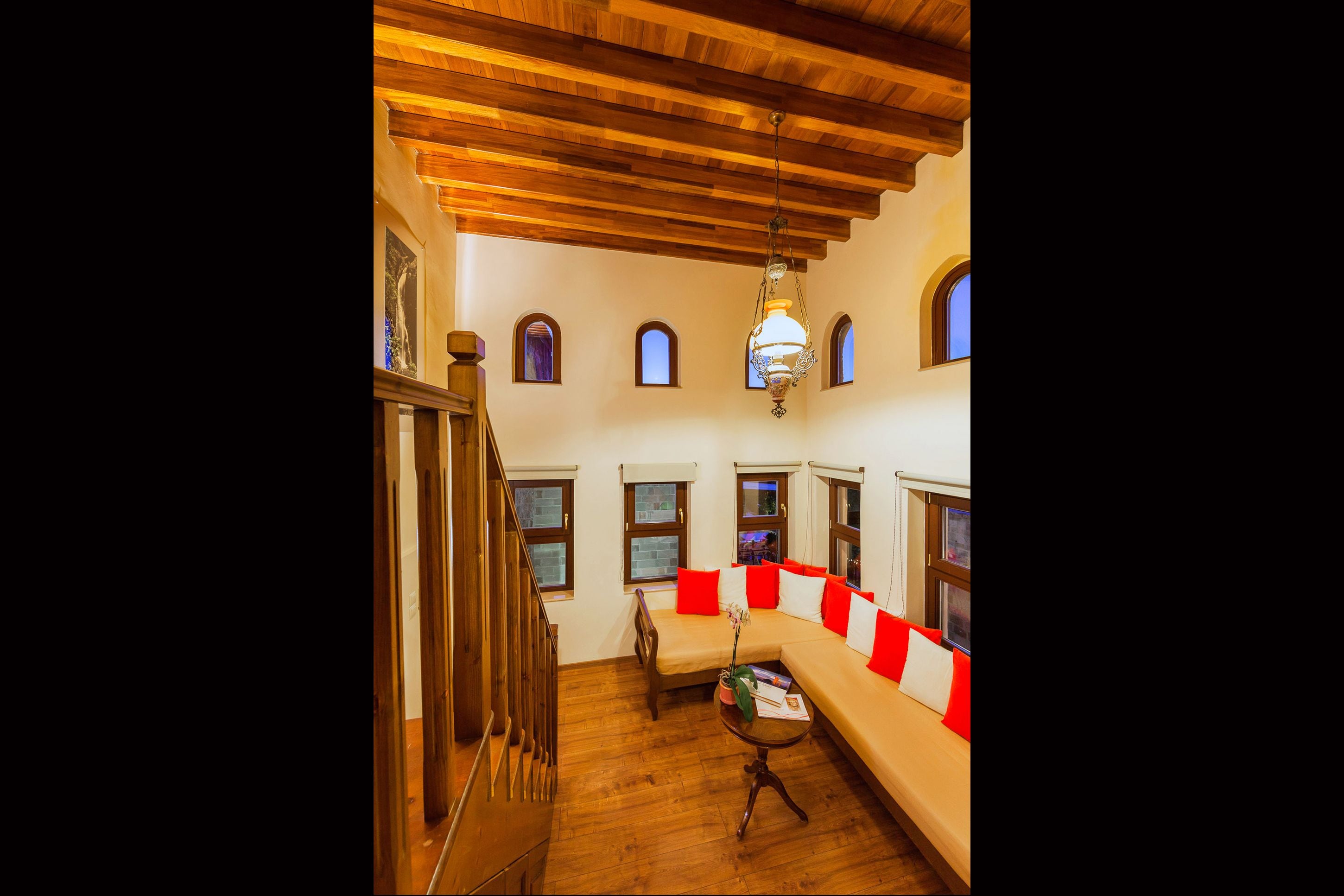 Um quarto amplo com teto de madeira, um sofá com almofadas vermelhas, piso de madeira e uma escada.