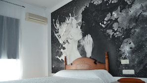 Quarto com cama, mesa de cabeceira e um mural na parede.