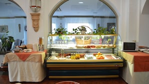 Um buffet de café da manhã com diversas opções de comida e bebidas, um relógio na parede e uma janela com vista.