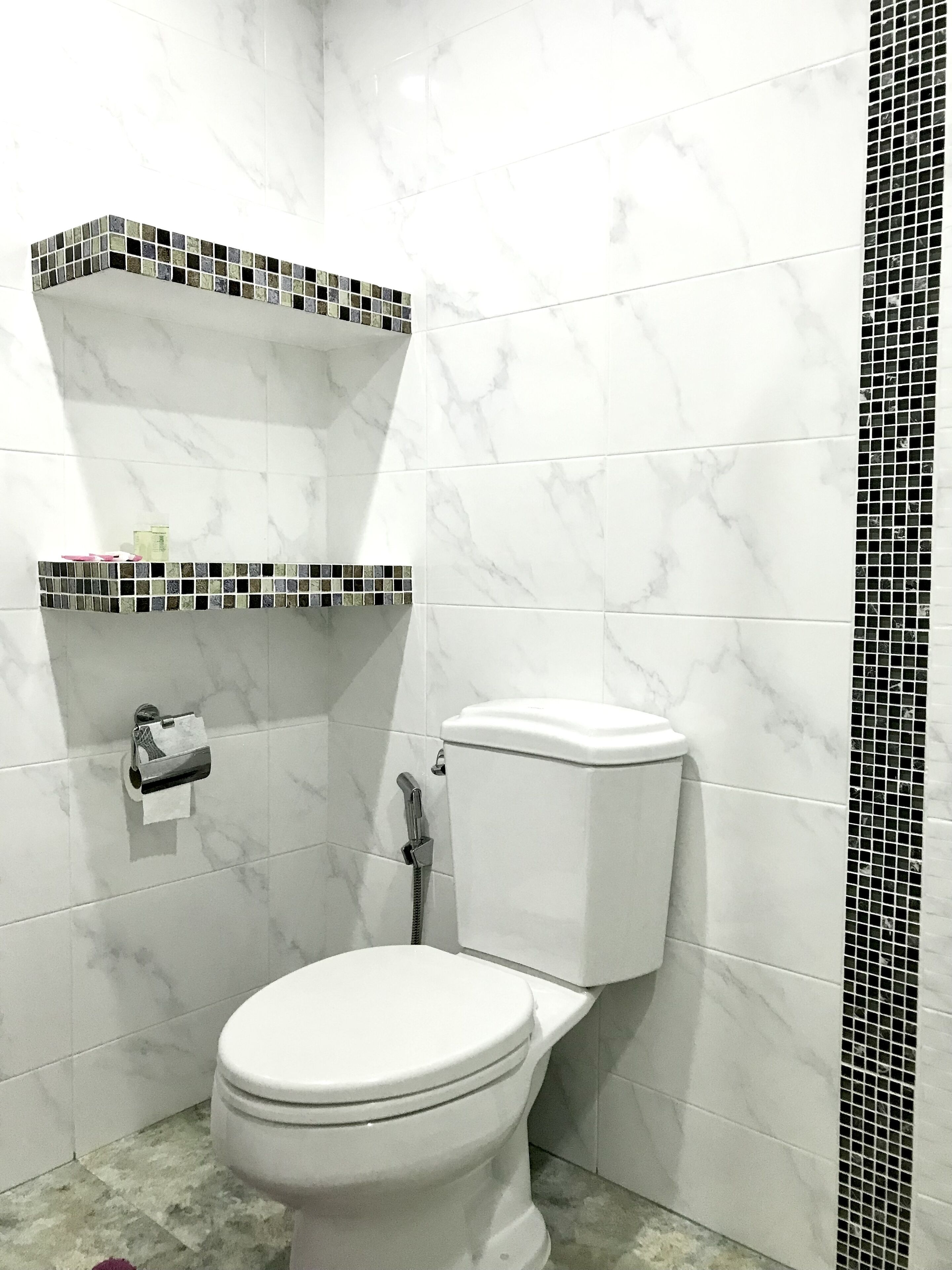 Casa de banho com sanita, chuveiro e parede revestida a azulejos.