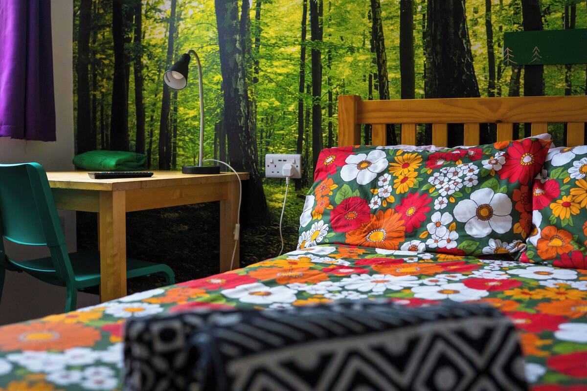Quarto com cama, escrivaninha, cadeira e parede com painel de floresta.