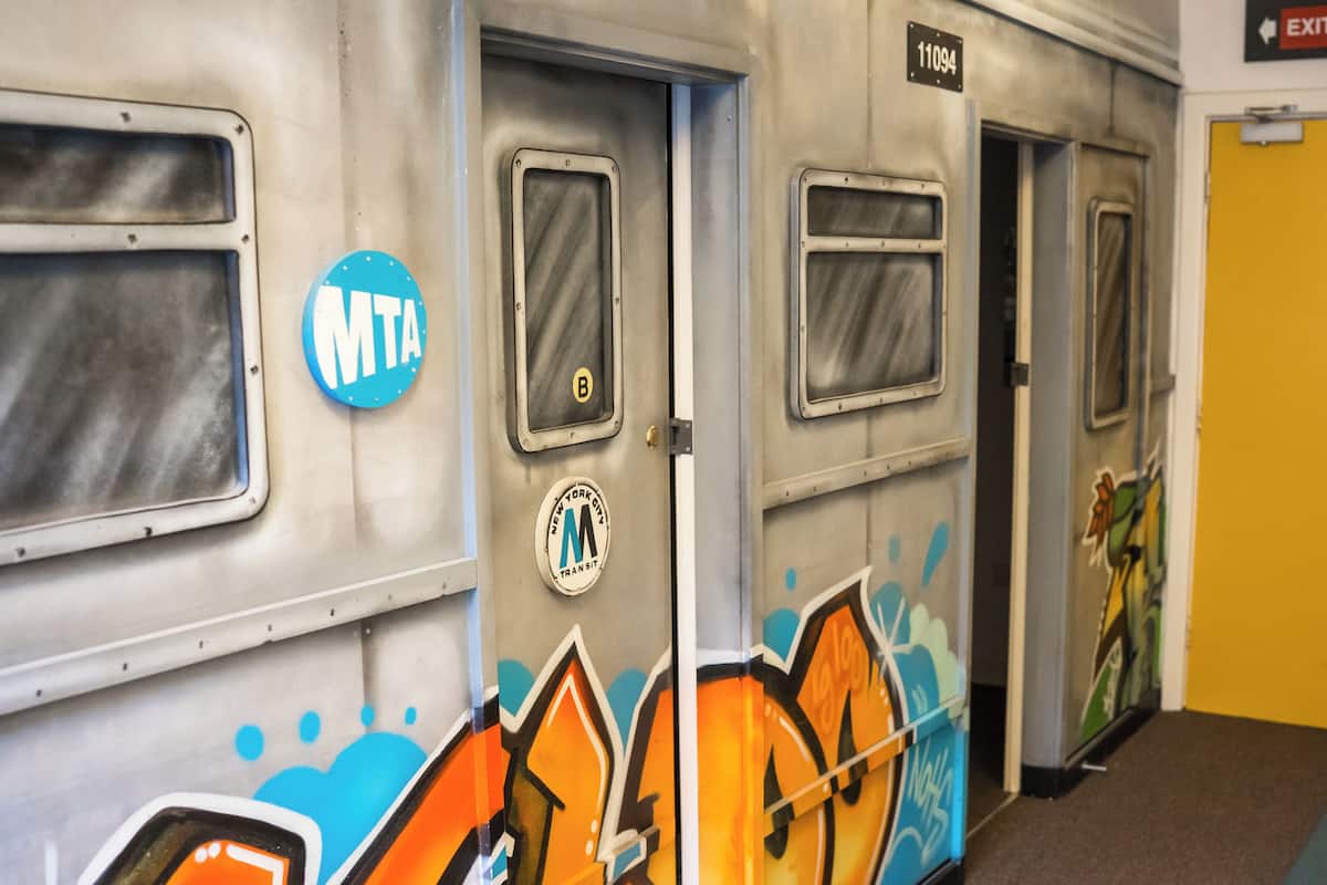 Interior de um vagão de metrô com grafites, uma placa azul da MTA e uma porta de saída amarela.