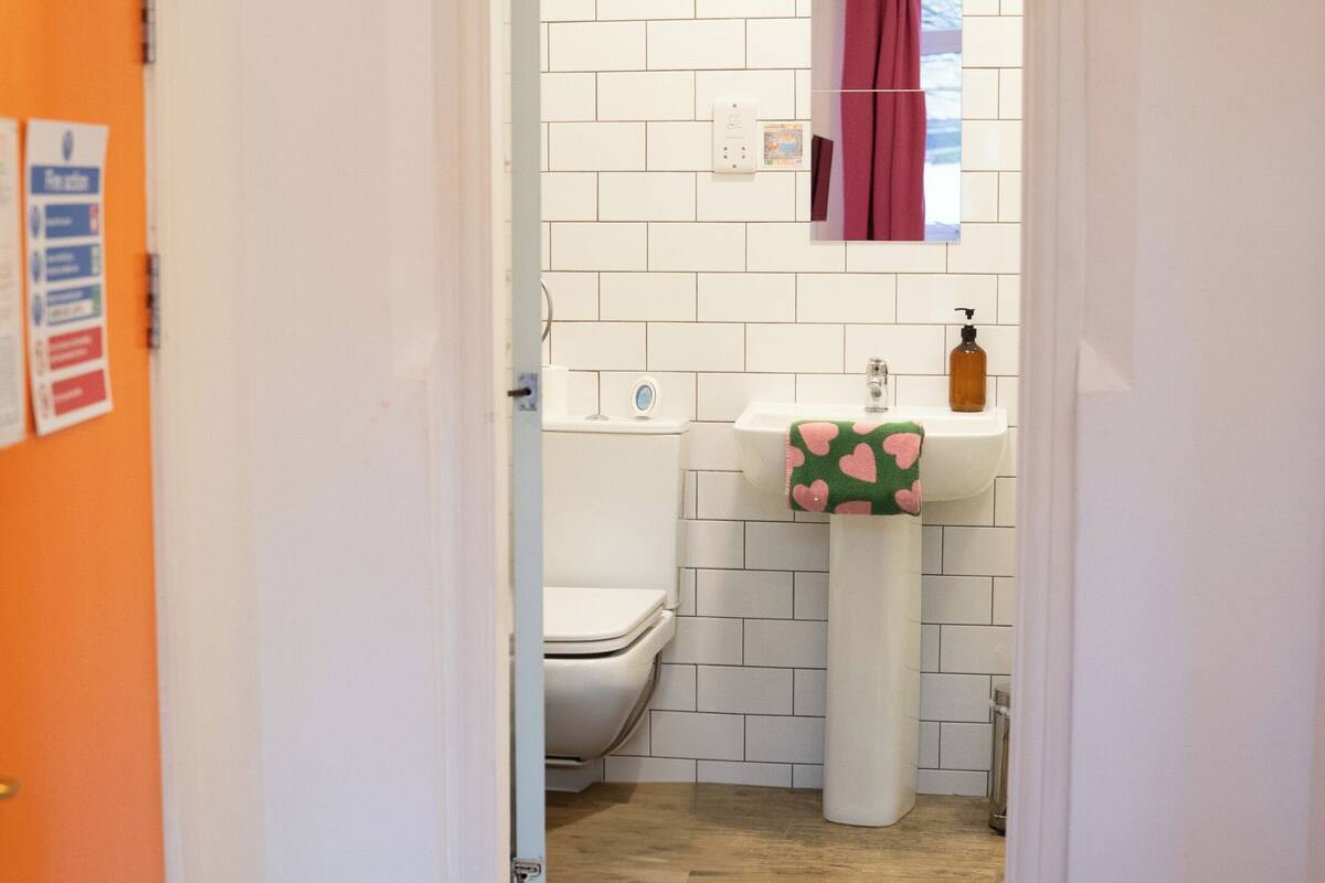 Corredor que leva a um banheiro com vaso sanitário, pia e porta-toalhas.