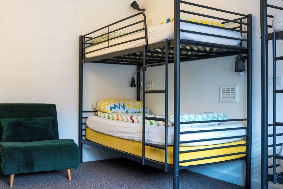 Uma cama de solteiro com uma cadeira verde e uma mesa amarela em um quarto com paredes brancas.