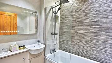 Uma casa de banho moderna com chuveiro de vidro, lavatório branco e toucador de madeira.