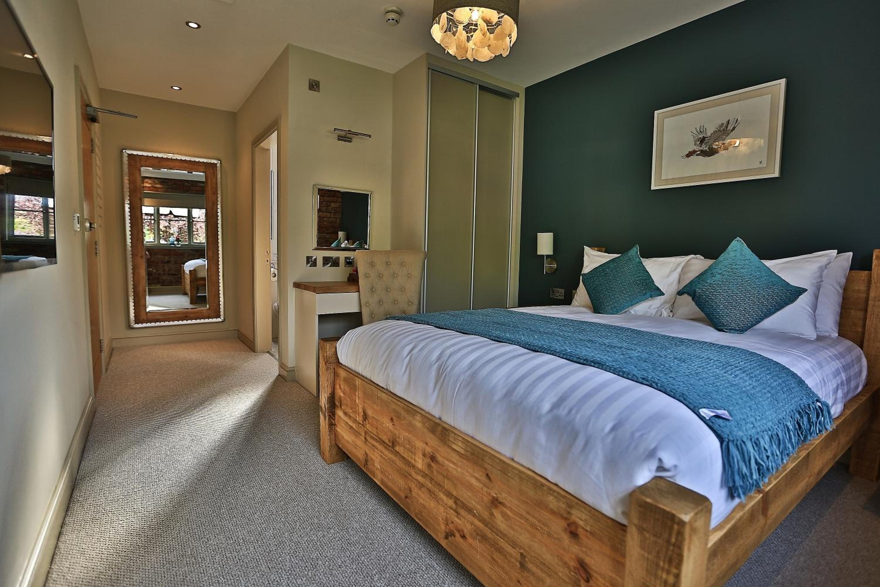 Quarto com cama de madeira, um espelho grande, uma escrivaninha e parede verde.