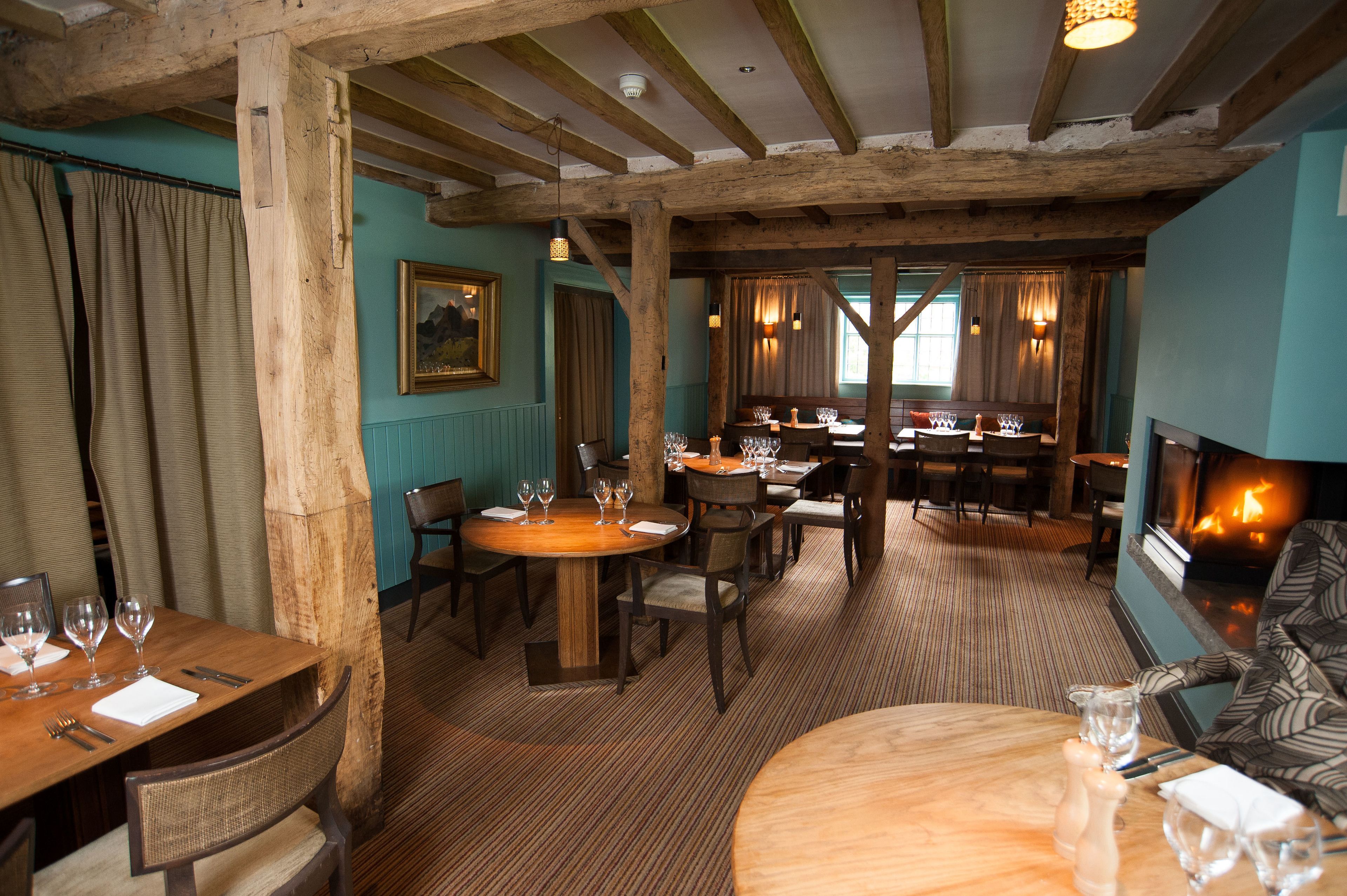 Um restaurante acolhedor com vigas de madeira, lareira e várias mesas de jantar.