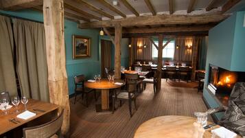 Um restaurante acolhedor com vigas de madeira, lareira e várias mesas de jantar.