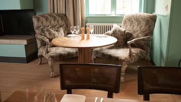 Uma área de refeições com duas poltronas estampadas, uma mesa redonda de madeira e uma mesa posta com talheres e copos.
