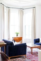 Quarto nos fundos com duas poltronas azuis, uma mesa de centro de madeira e um tapete estampado.