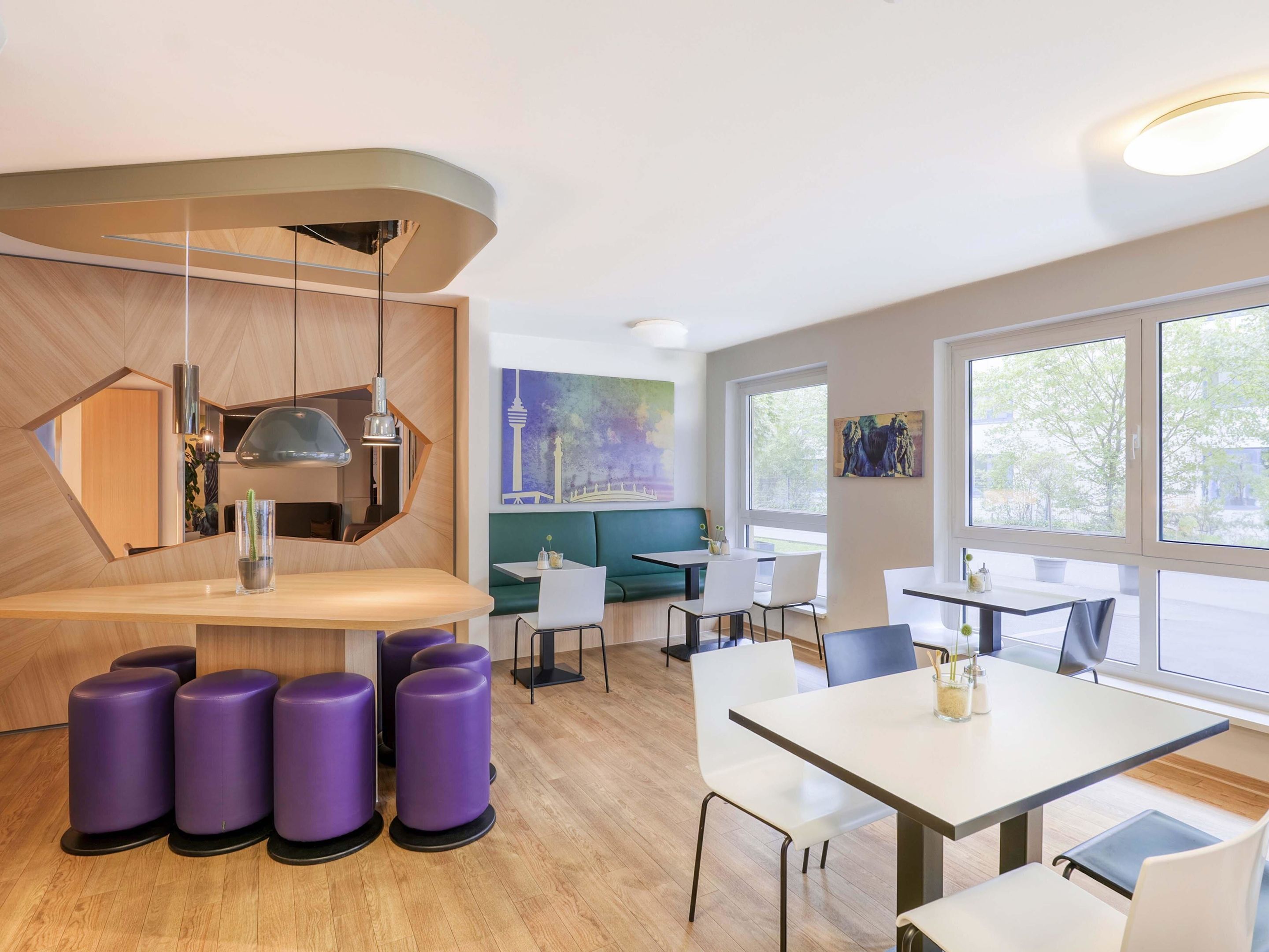 Uma sala de jantar moderna com piso de madeira, banquetas roxas e um assento fixo verde.