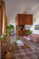 Uma sala de estar com piso xadrez, uma estante de madeira, um sofá, uma mesa de centro e plantas em vasos.