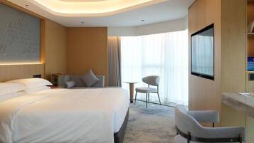 Quarto de hotel com uma cama grande, uma escrivaninha, uma cadeira e uma televisão.