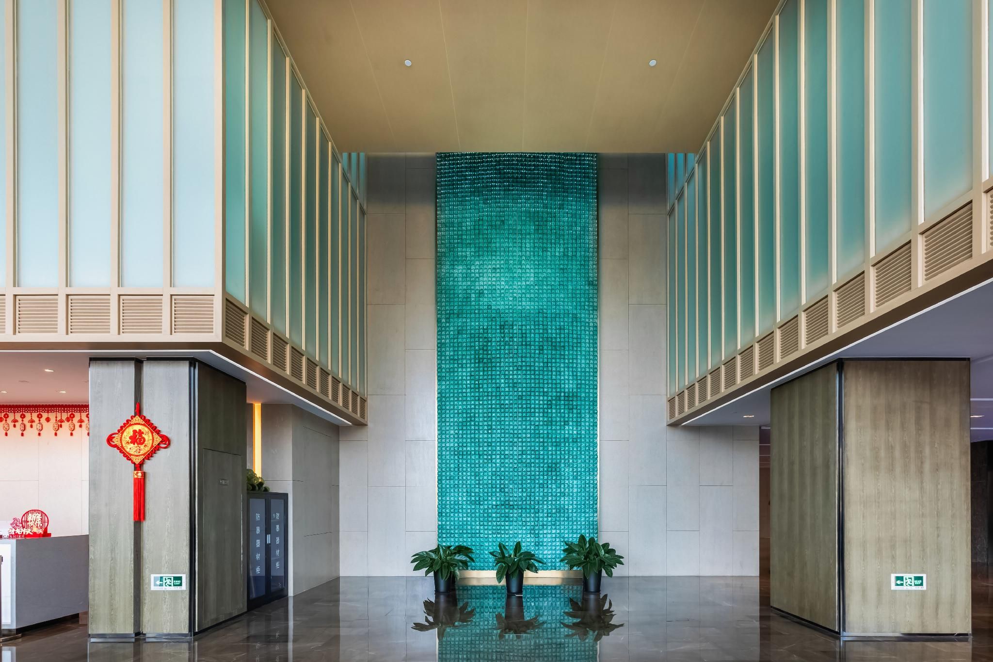 Um hall amplo com um grande painel decorativo vertical, um balcão de recepção e plantas em vasos.