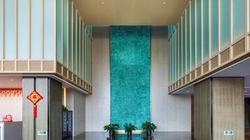 Um hall amplo com um grande painel decorativo vertical, um balcão de recepção e plantas em vasos.