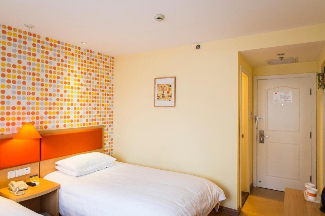 Quarto de hotel com cama, mesa de cabeceira com abajur, parede com padrão de bolinhas e porta com placa.