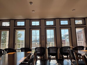 Uma sala de conferências com uma mesa comprida e várias cadeiras, janelas amplas com persianas e iluminação embutida no teto.