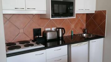 Cozinha compacta com armários brancos, micro-ondas preto, fogão, torradeira, chaleira e lava-louças Samsung.
