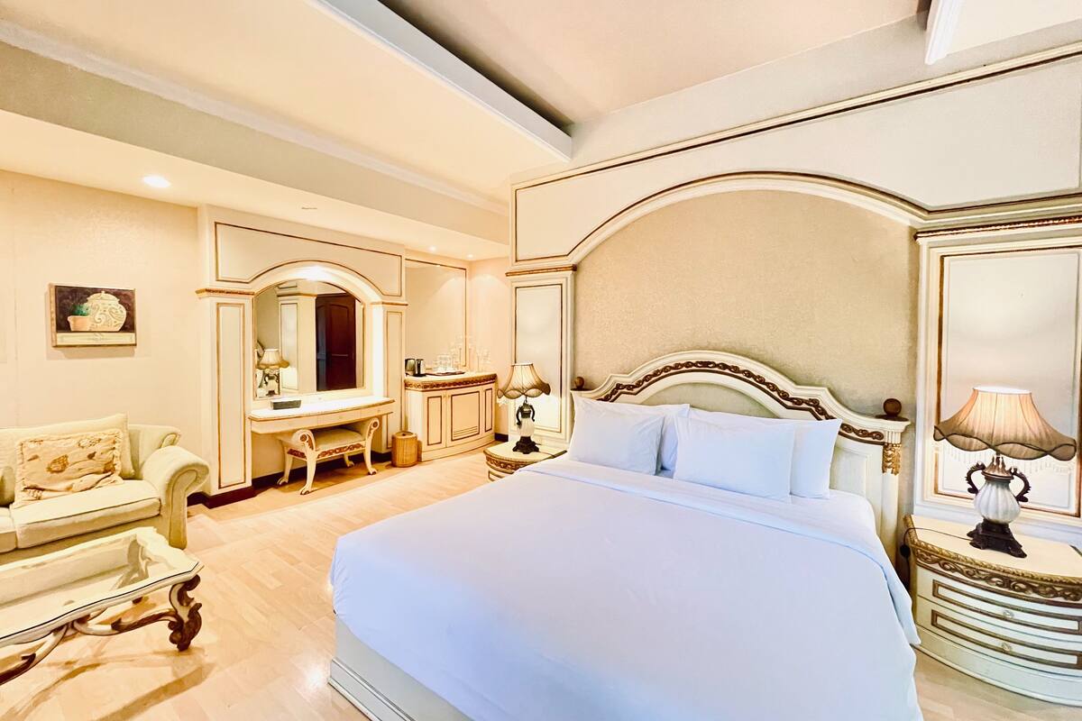 Quarto de hotel com uma cama grande, uma escrivaninha com espelho, uma cadeira, um aparador e uma mesa de cabeceira com abajur.