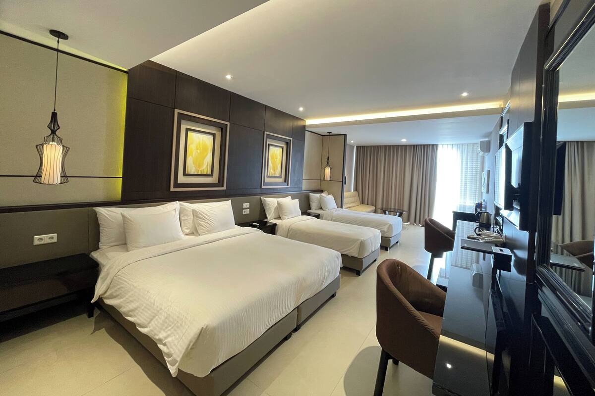 Quarto de hotel com duas camas, uma mesa, uma cadeira, televisão e obras de arte nas paredes.