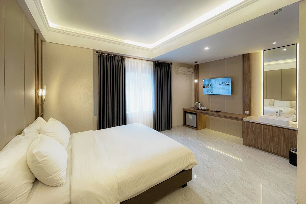 Quarto de hotel com uma cama grande, televisão, banheiro com espelho e escrivaninha.