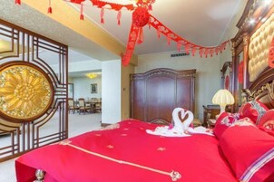 Quarto de hotel com colcha vermelha, painel decorativo na parede e guarda-roupa de madeira.