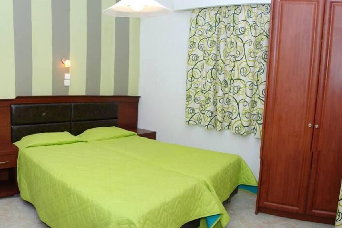 Quarto com cama, mesas de cabeceira, guarda-roupa e luminária na parede.