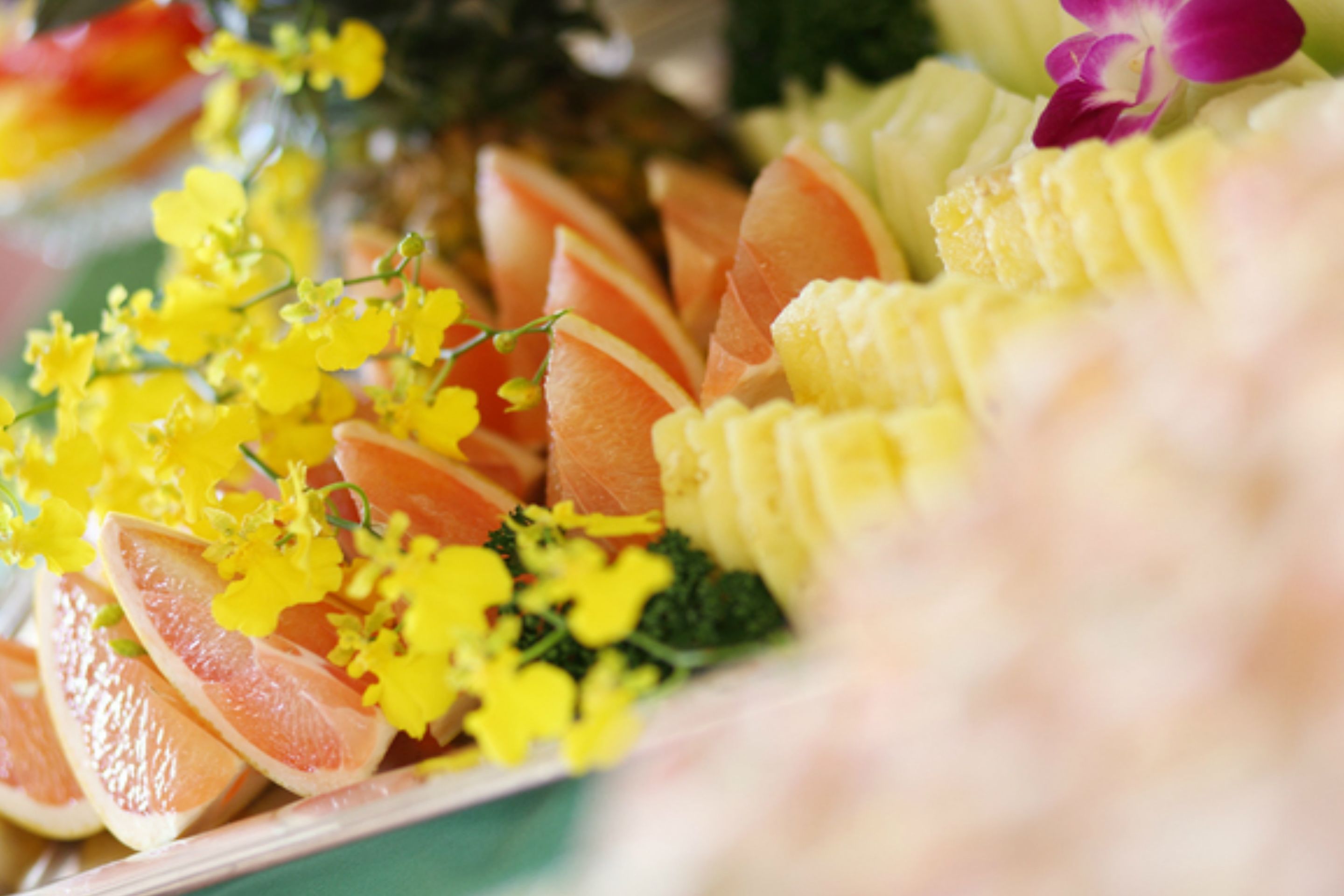 Close-up de uma tábua de frutas com laranjas fatiadas, bananas e uma flor.