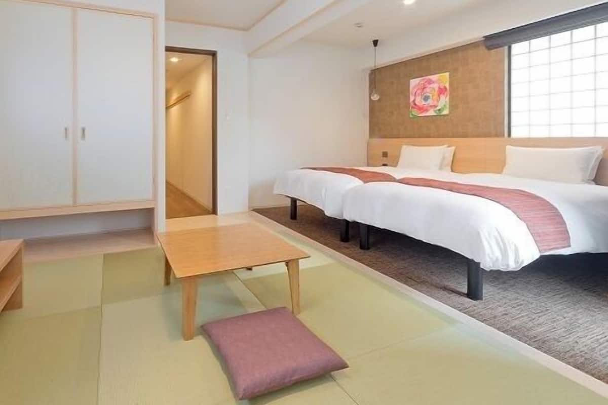 Quarto de hotel com uma cama, uma mesinha, uma cadeira, um travesseiro e um quadro na parede.