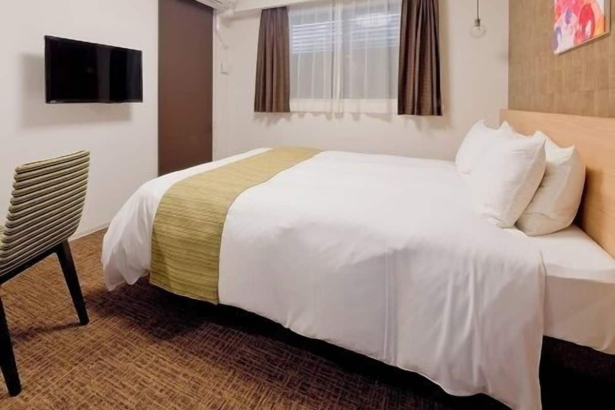 Quarto de hotel com cama, uma cadeira, televisão de tela plana, ar condicionado, janela com cortinas e um quadro na parede.