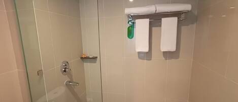 Um banheiro moderno com box de vidro, um porta-toalhas com duas toalhas brancas e uma pequena prateleira com artigos de higiene pessoal.