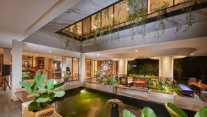 Amplo espaço interno com um elemento central de água, áreas de estar e vegetação exuberante.