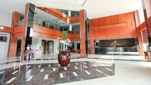 Um lobby de hotel moderno, com um balcão de recepção espaçoso, um vaso decorativo com flores e um chão de mármore polido.