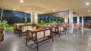 Amplo espaço interno com diversos arranjos de assento, incluindo sofás e mesas, cercado por plantas em vasos.