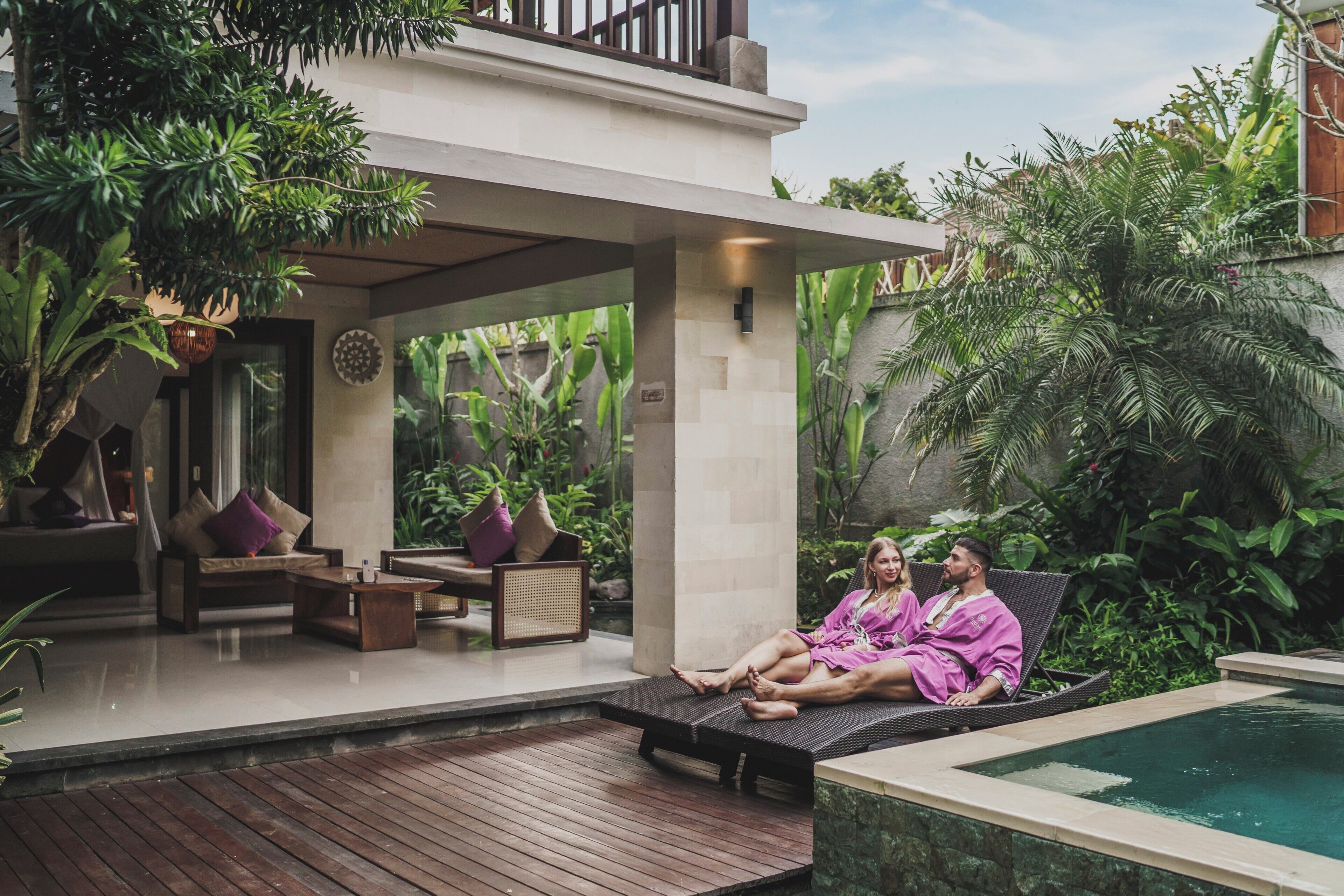 Uma área de estar externa moderna com piscina, espreguiçadeiras e um espaço coberto para relaxar, tudo cercado por vegetação exuberante.