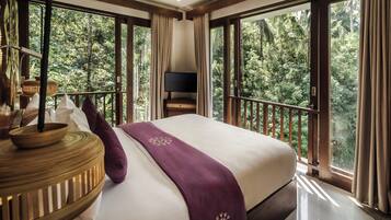 Quarto com uma cama grande, televisão e vista para uma floresta através de amplas janelas.