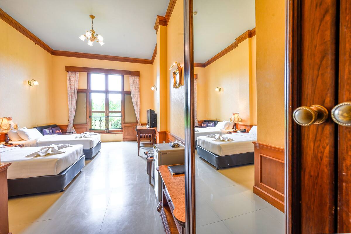 Quarto de hotel com duas camas, uma escrivaninha, uma cadeira, uma televisão e uma janela grande com cortinas.