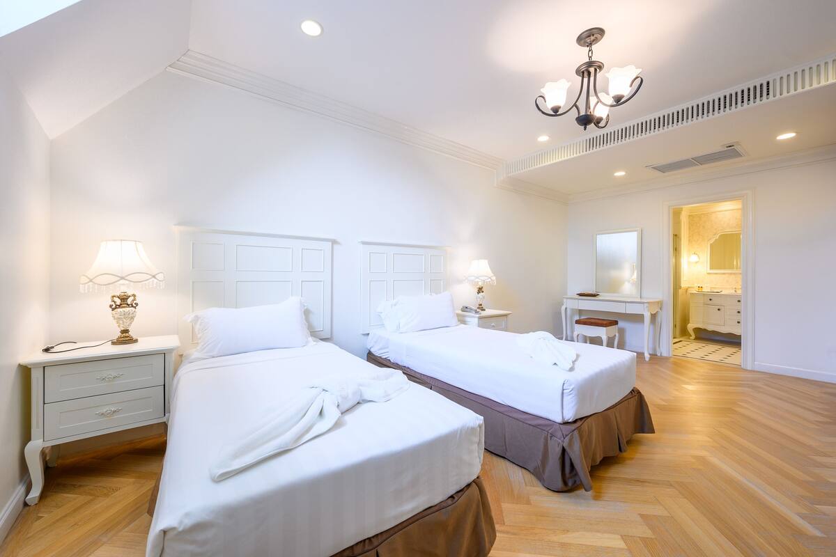 Quarto de hotel com duas camas, uma escrivaninha e uma cadeira.