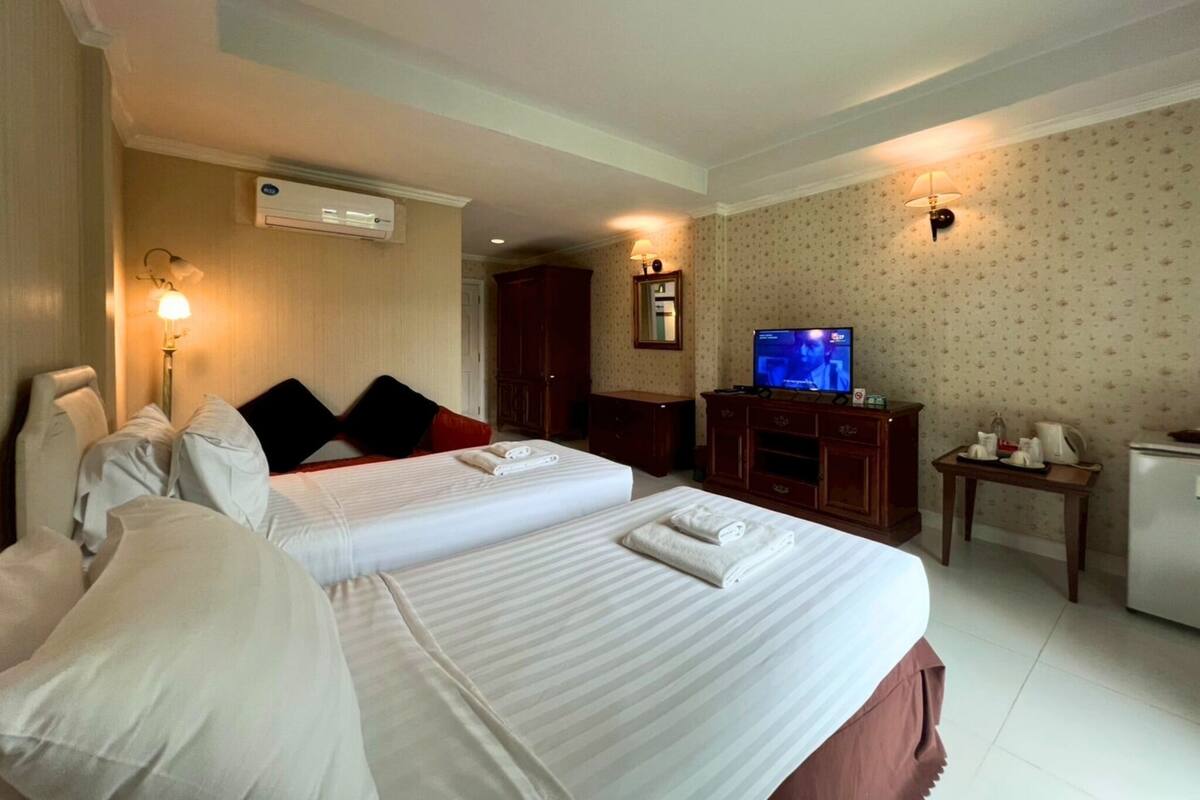 Quarto de hotel com duas camas, televisão, secretária com candeeiro e um guarda-roupa.