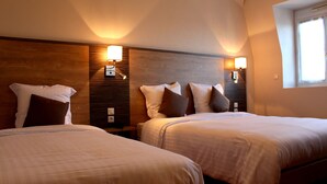 Quarto de hotel com duas camas, cabeceiras de madeira, luminárias e uma janela.